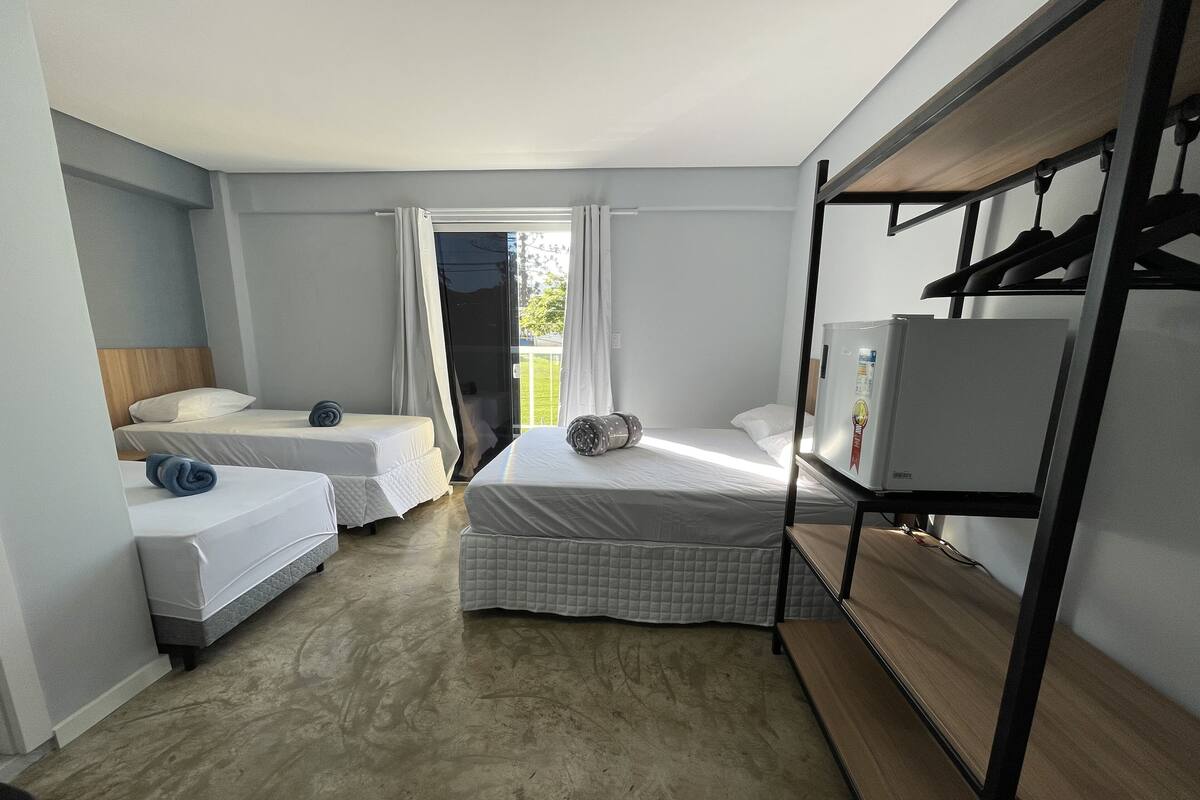 Quarto de hotel com duas camas, um guarda-roupa e vista para o exterior.