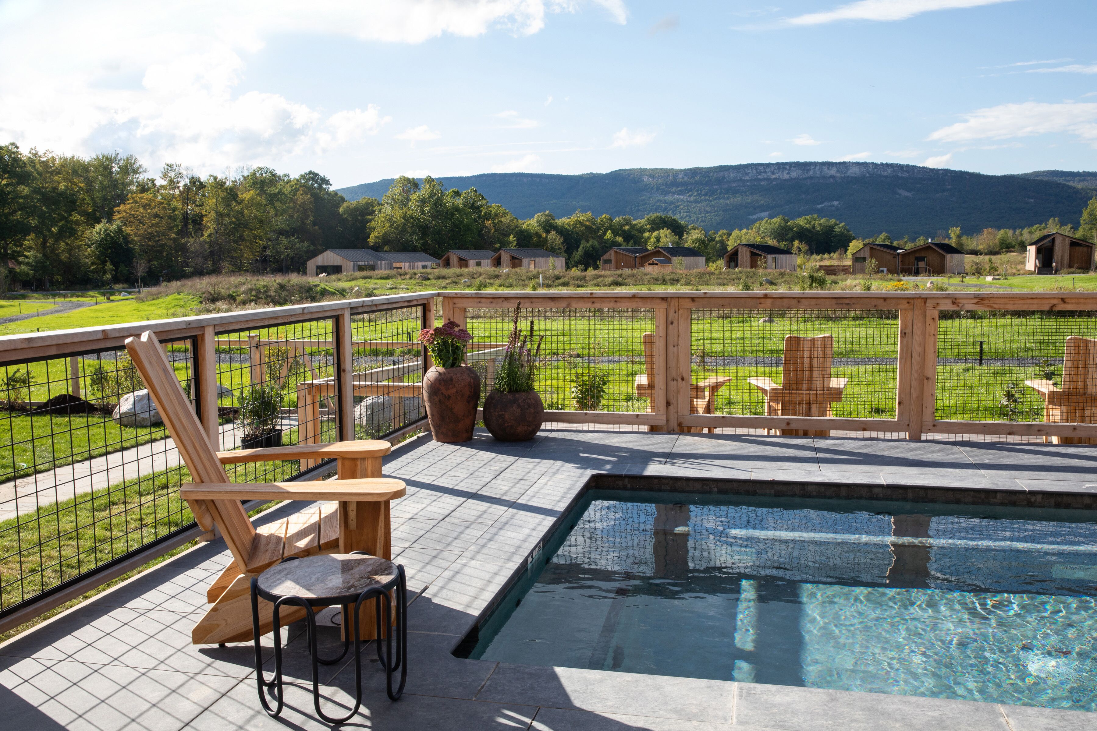 Área da piscina com vista para uma paisagem montanhosa, deck de madeira e mobiliário externo.