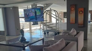 Um lobby moderno com uma grande TV de tela plana, área de estar com sofás e um painel decorativo na parede.
