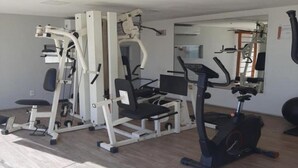 Academia com diversos equipamentos de exercício, incluindo uma máquina de musculação, um banco de imprensa e um aparelho elíptico.