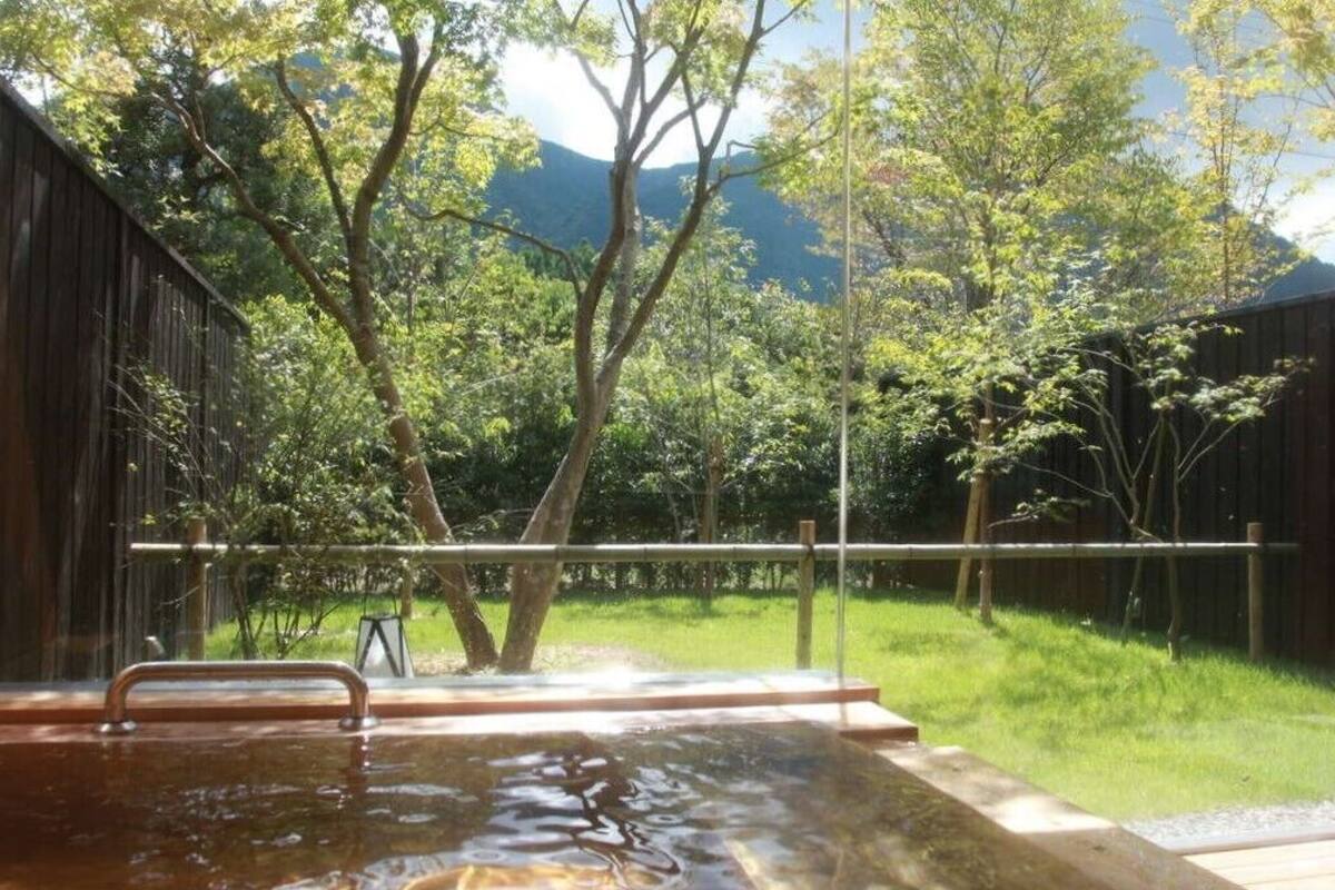Uma banheira de hidromassagem com vista para uma área gramada e árvores, um cercado de madeira e uma montanha ao fundo.
