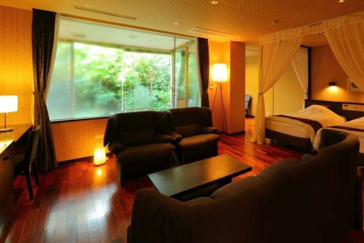 Quarto de hotel com uma grande janela, cama com dossel, um sofá e uma pequena mesa.
