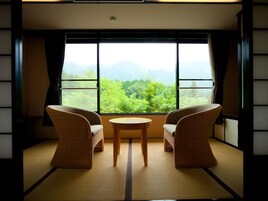 Quarto com duas cadeiras de vime e uma mesa pequena, janelas amplas com vista para colinas verdes.