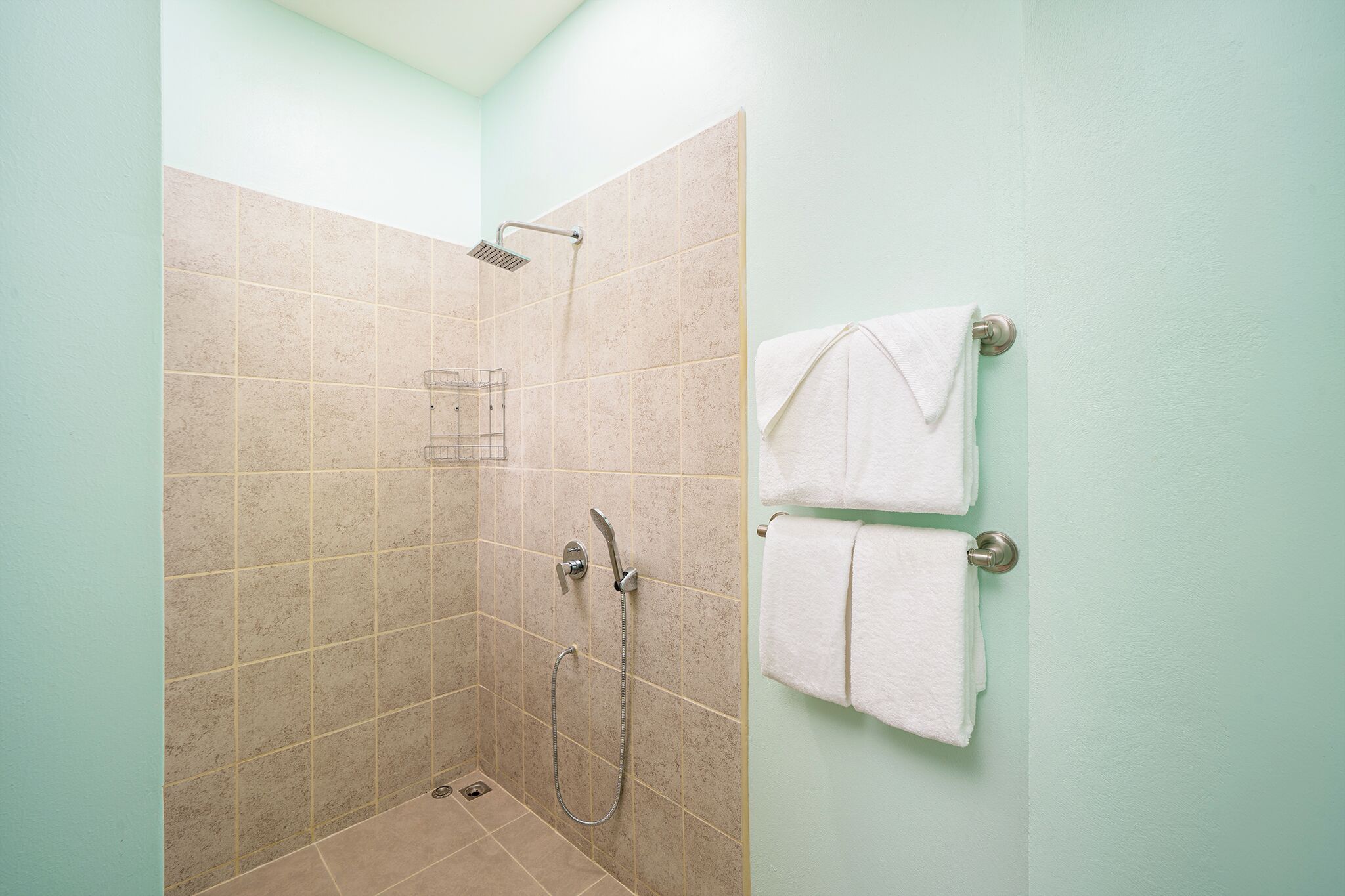 Um chuveiro com azulejos bege, um porta-sabonete de vidro e duas toalhas brancas penduradas em uma barra de metal.