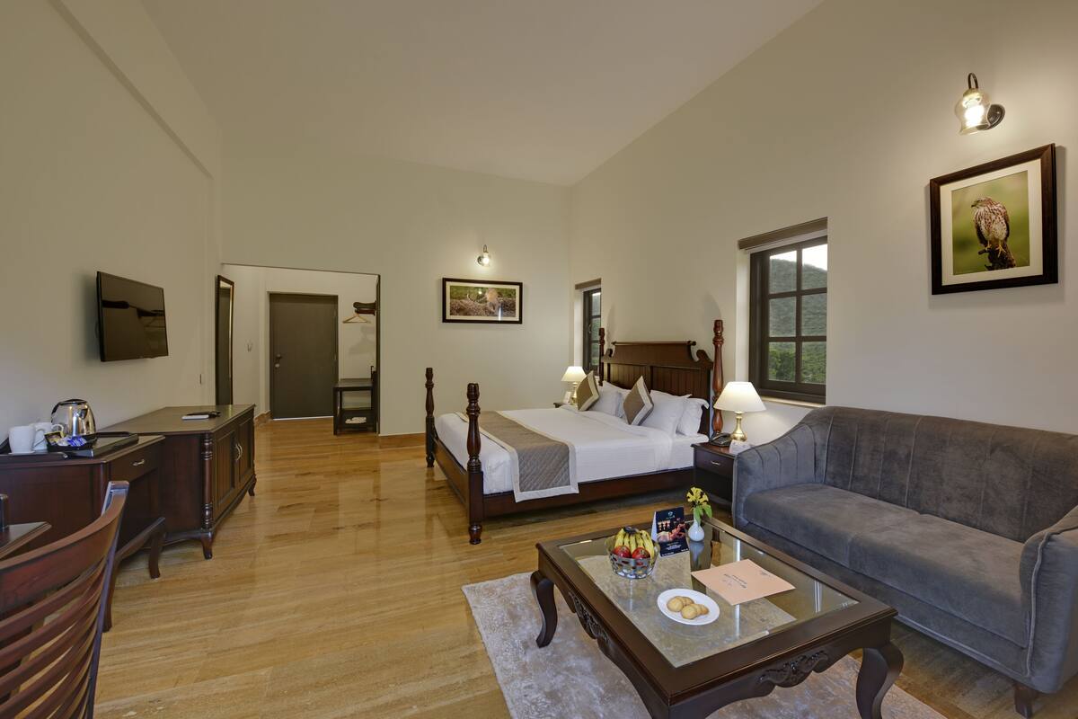 Quarto de hotel com cama, sofá, mesa de jantar e televisão.