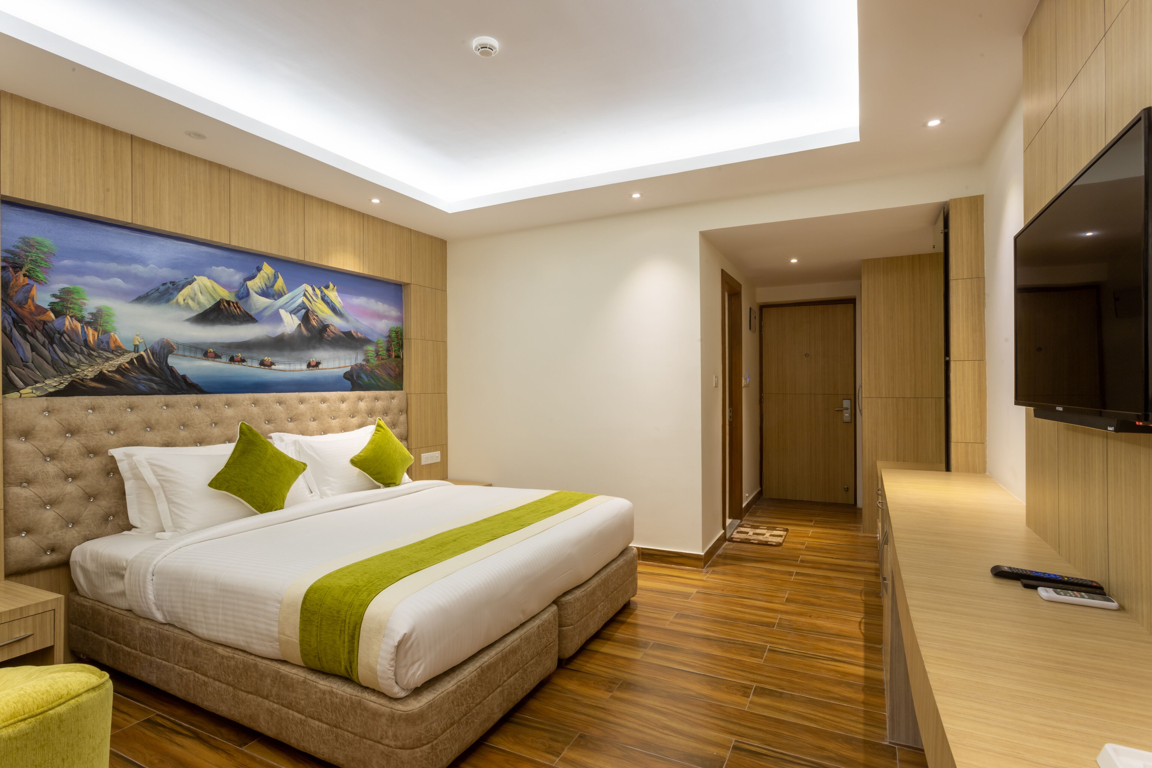 Quarto de hotel moderno com uma cama grande, um quadro de uma paisagem montanhosa, televisão de tela plana e piso de madeira.