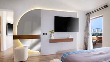 Quarto de hotel moderno com uma televisão de tela plana grande presa na parede, uma cama de madeira, um pequeno espaço de estar e vista para a cidade através de uma janela.
