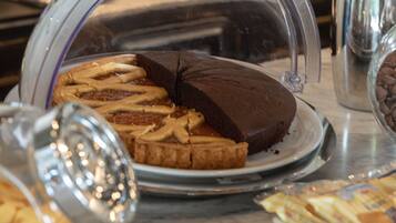 Exposição de sobremesas com um bolo de chocolate, uma cúpula de vidro e uma garrafa de molho sobre um balcão de mármore.