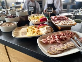 Buffet com diversas opções de comida, incluindo carnes, queijos e frutas.