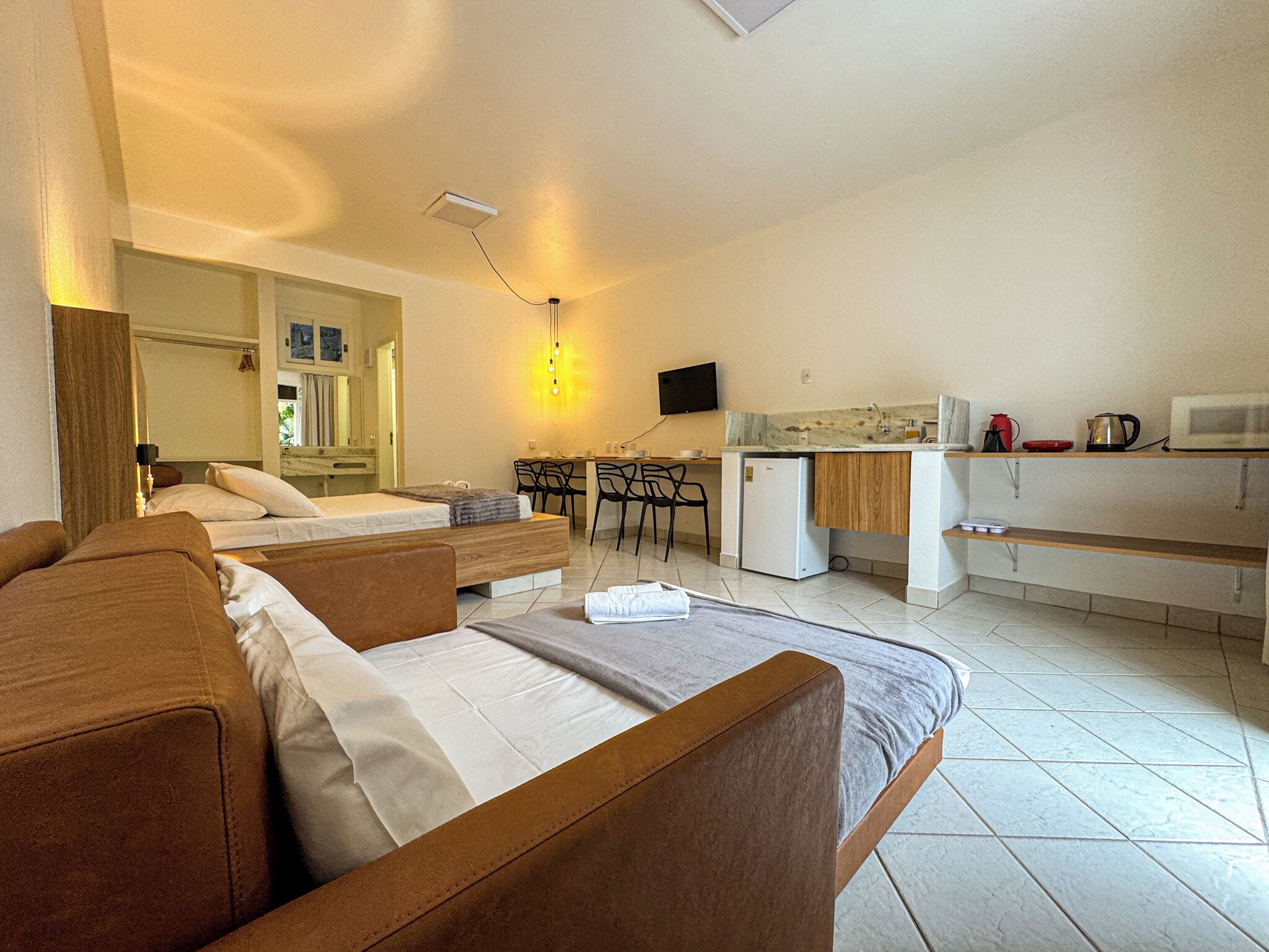 Quarto de hotel com cama, escrivaninha, cozinha compacta e banheiro.