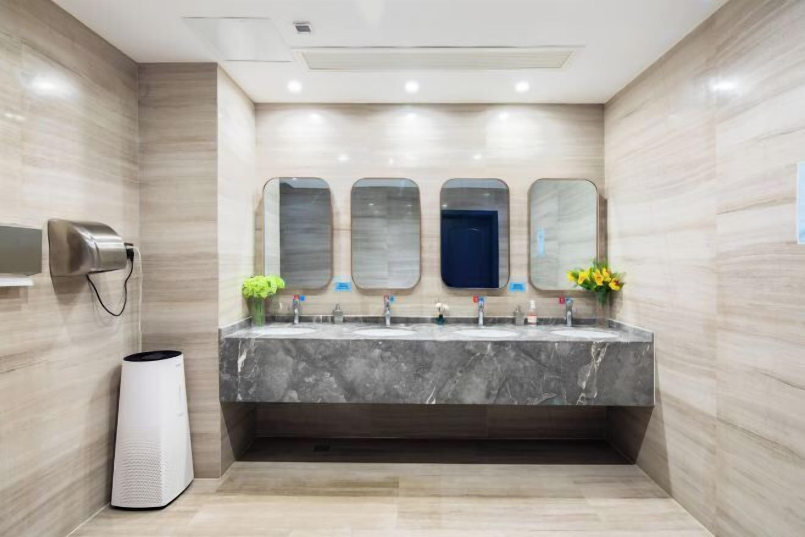 Casa de banho moderna com lavatório de mármore, três espelhos e secador de mãos.