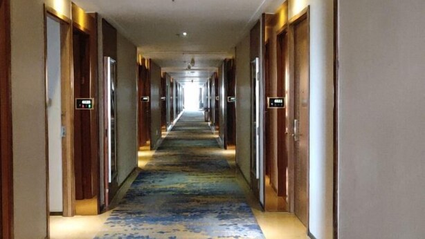 Corredor de hotel com piso revestido de carpete, portas de madeira e luminária no teto.