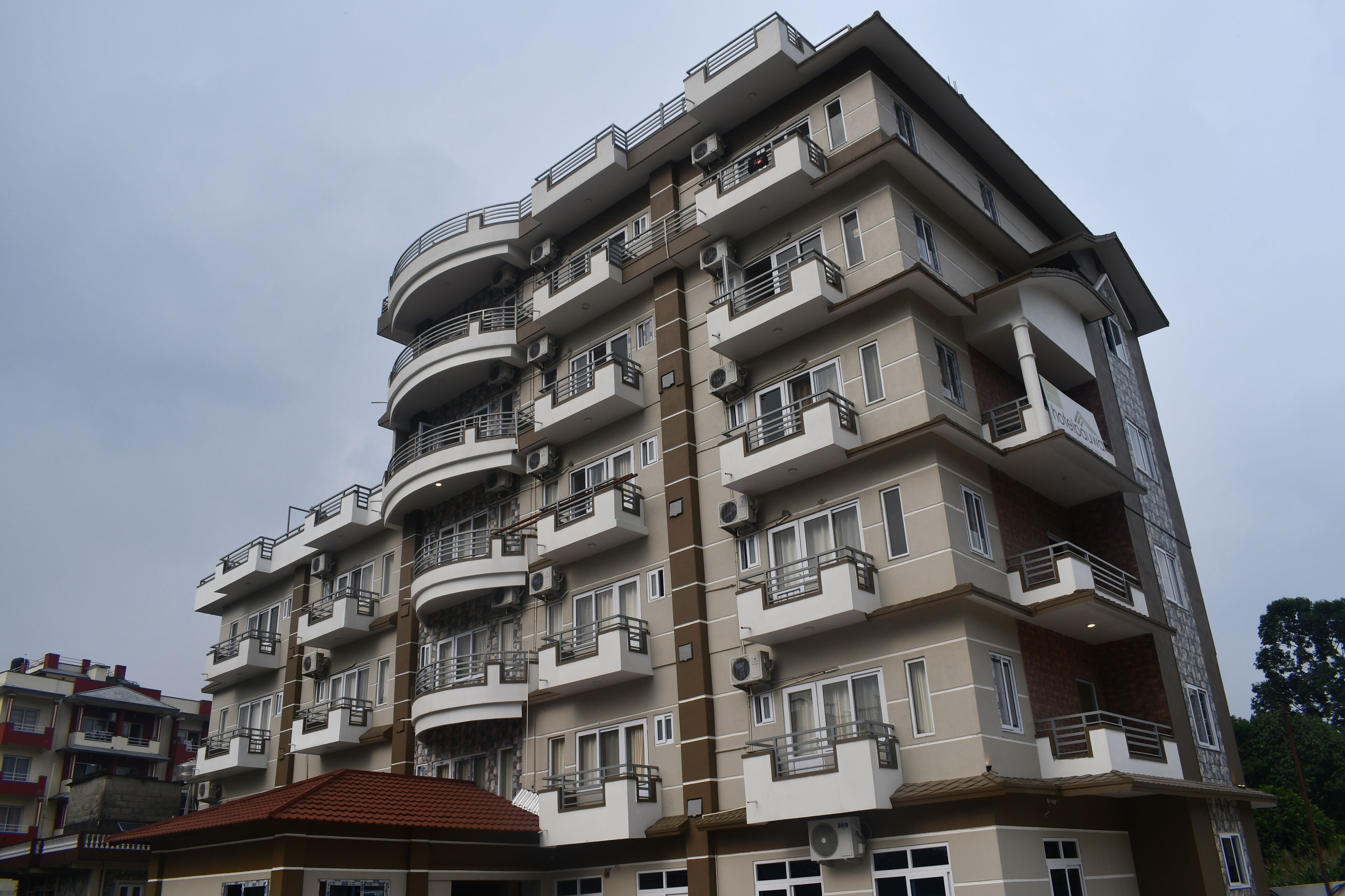 Um edifício residencial com várias andares, varandas, aparelhos de ar condicionado e telhado de telhas vermelhas.