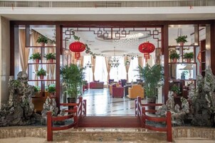 Um hall tradicional em estilo chinês, com um caminho de pedra que leva a áreas de estar, decorado com lanternas vermelhas e plantas em vasos.