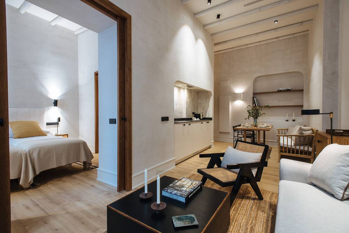 Quarto moderno e bem iluminado com cama, área de refeições e cozinha compacta.