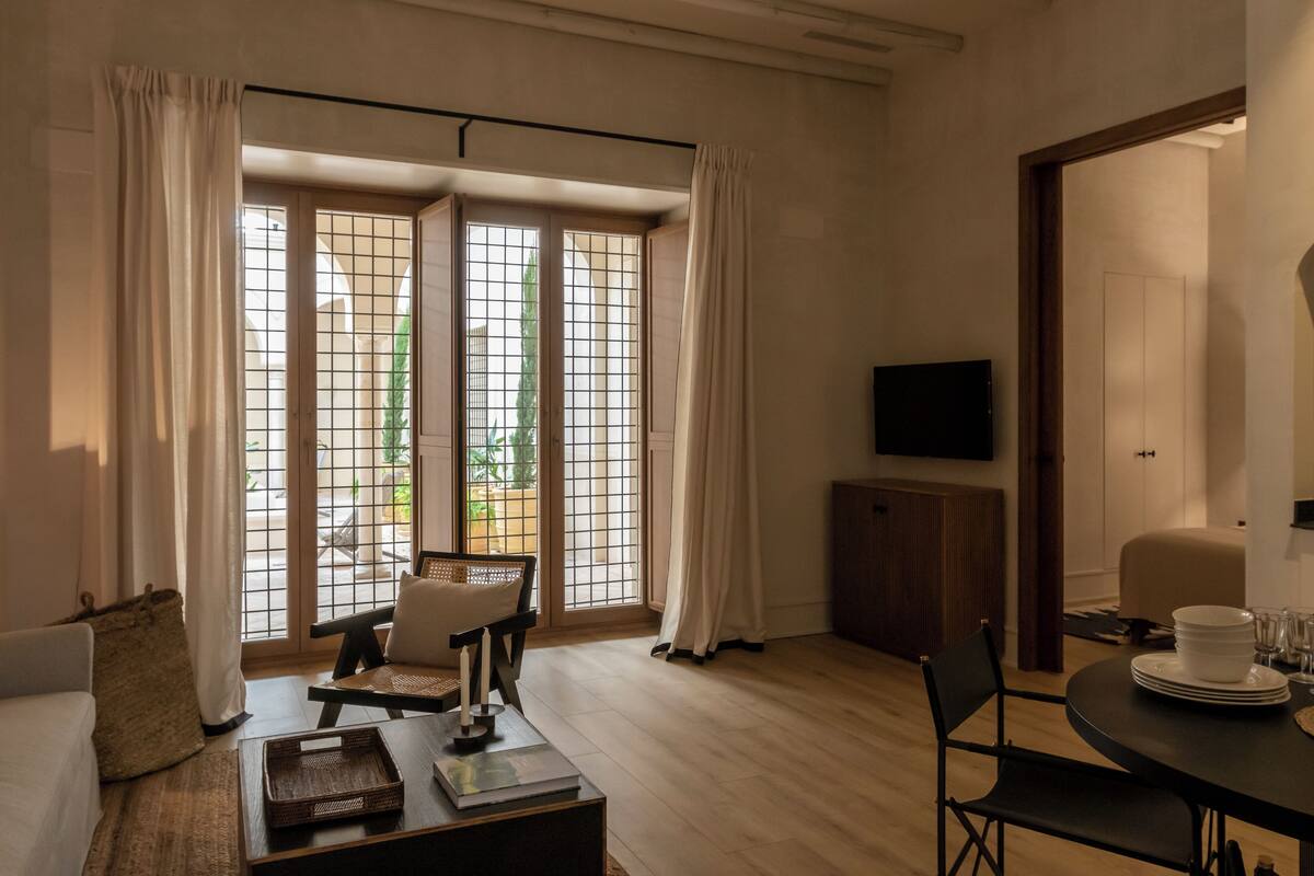 Uma ampla sala de estar com uma grande porta de vidro deslizante, uma televisão de tela plana, uma mesa de jantar com pratos e copos, e um espaço de estar confortável com sofá e poltronas.