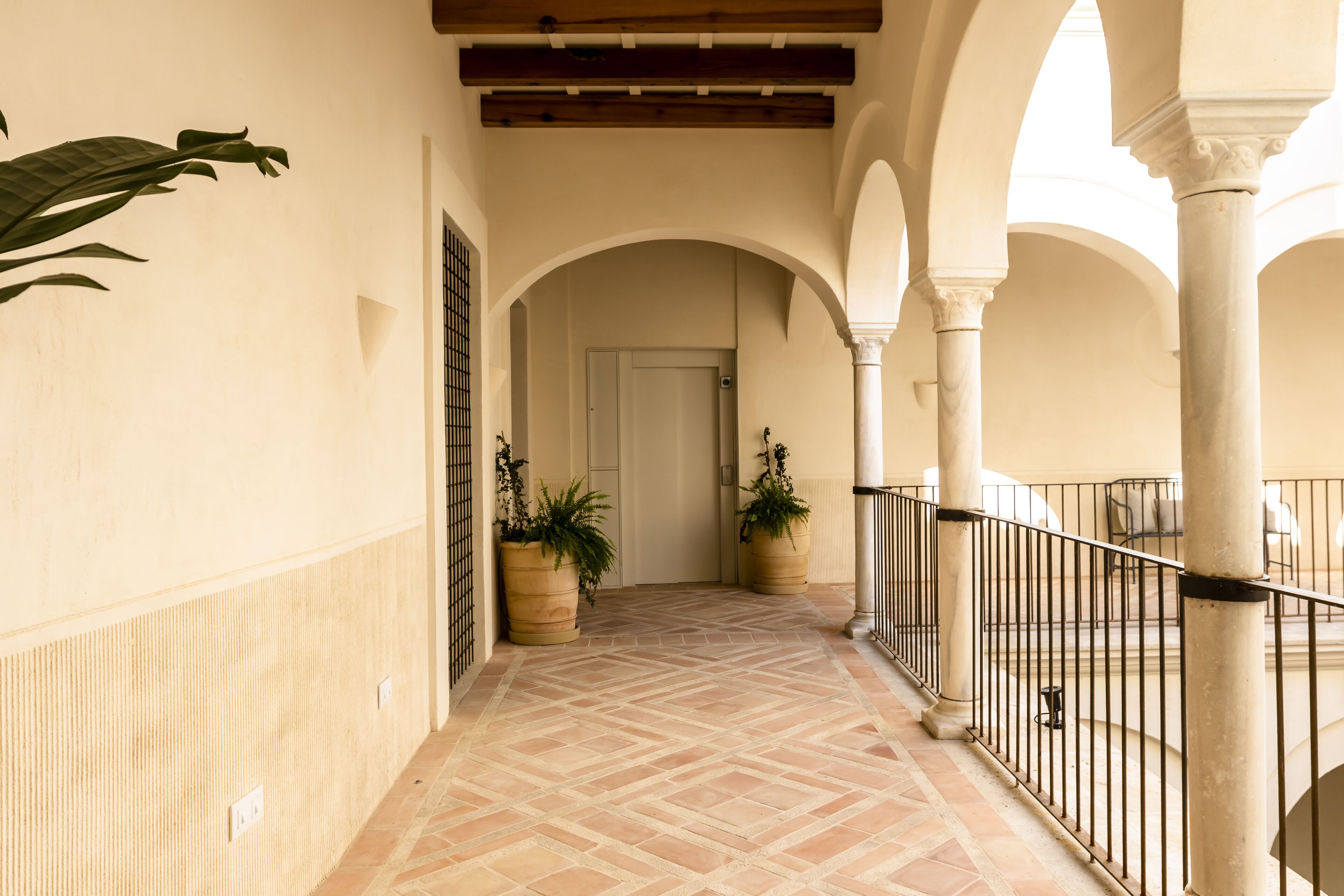 Um corredor coberto com piso de azulejos, arcos e plantas em vasos.