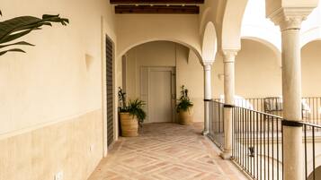 Um corredor coberto com piso de azulejos, arcos e plantas em vasos.
