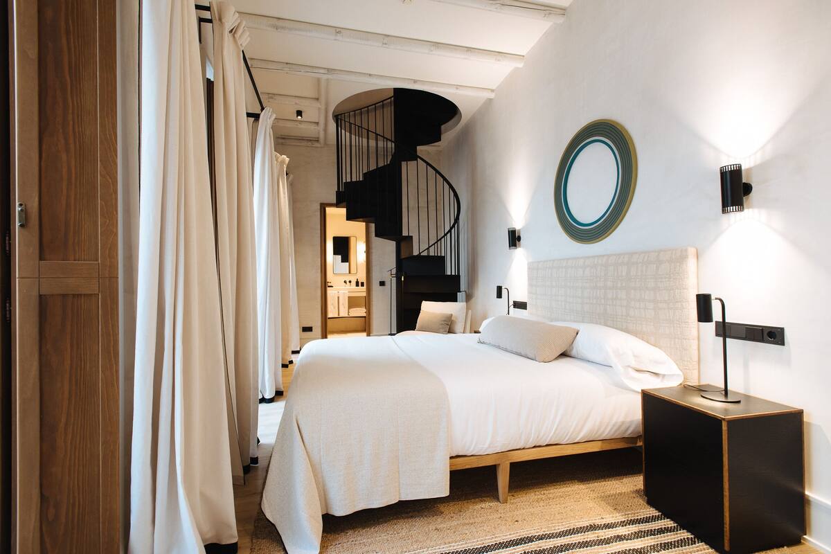 Um quarto moderno com uma cama grande, uma escada em espiral e um espelho redondo na parede.