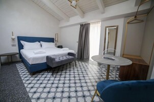 Quarto de hotel com cama, uma mesinha, uma cadeira, espelho e cabideiro.