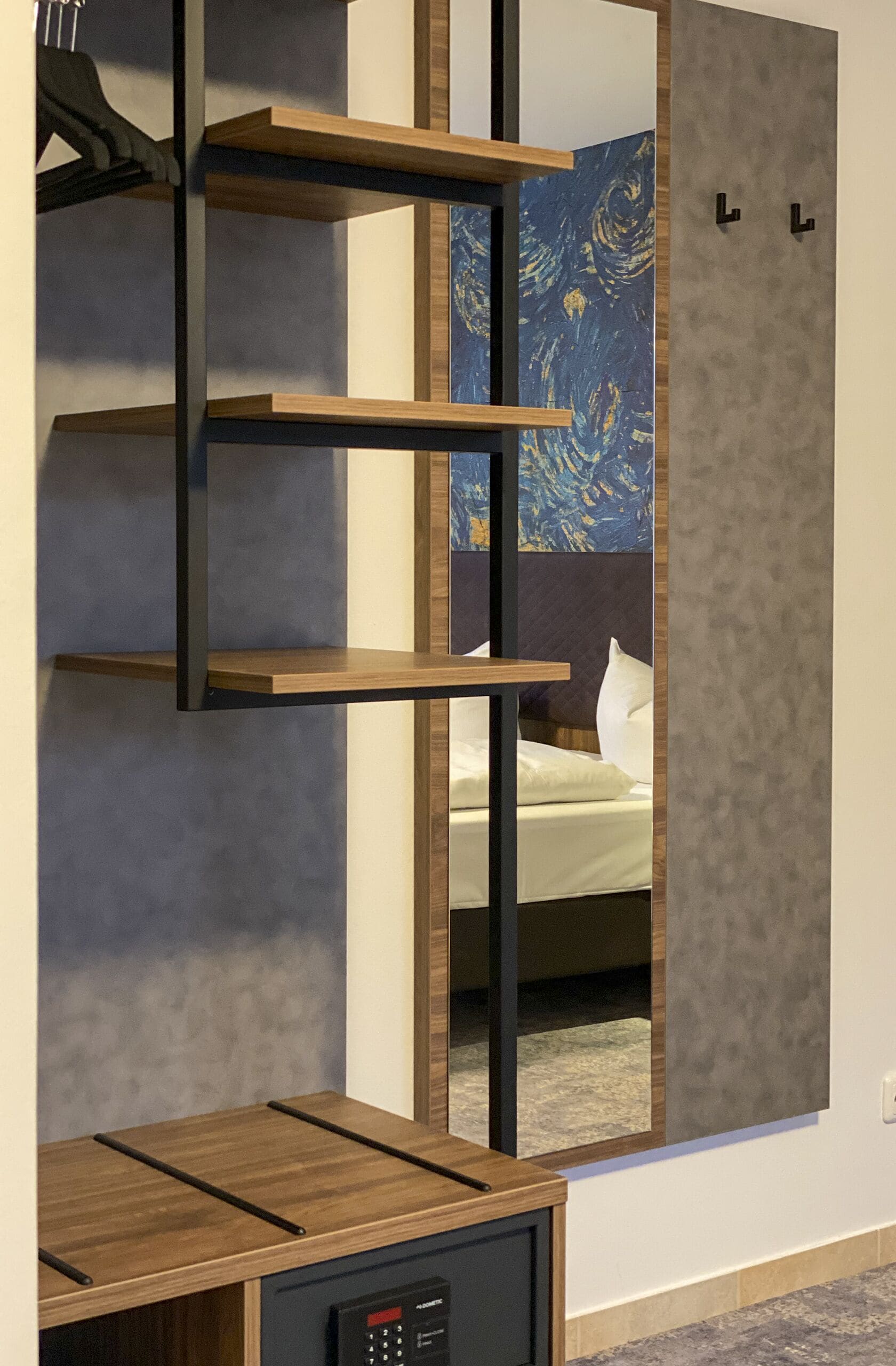 Quarto de hotel com escrivaninha de madeira, espelho e cama com roupa de cama branca.