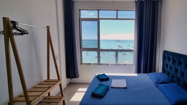 Quarto com uma janela ampla, cama com roupa de cama azul, escada de madeira e cabeceira azul.