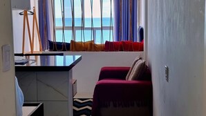Uma sala de estar moderna com um sofá vermelho, uma pequena cozinha e vista pela janela com cortinas.