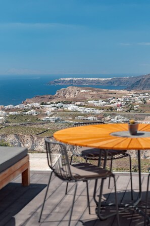 Terraço com mesa e cadeiras, com vista para uma cidade costeira, edifícios e o mar.