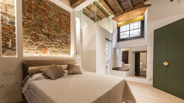 Quarto com cama grande, parede de tijolos, janela e porta verde.
