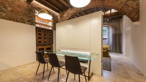 Uma área de refeições com mesa de vidro e cadeiras, um armário branco e uma parede de tijolos.