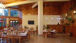 Interior de madeira com várias mesas e cadeiras de jantar, um balcão de recepção e plantas em vasos.