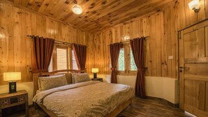 Quarto com painéis de madeira, uma cama grande, duas mesas de cabeceira com abajures e uma porta.