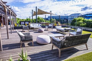 Um deck externo com móveis de vime, uma grande mesa redonda e uma estrutura de pérgola.