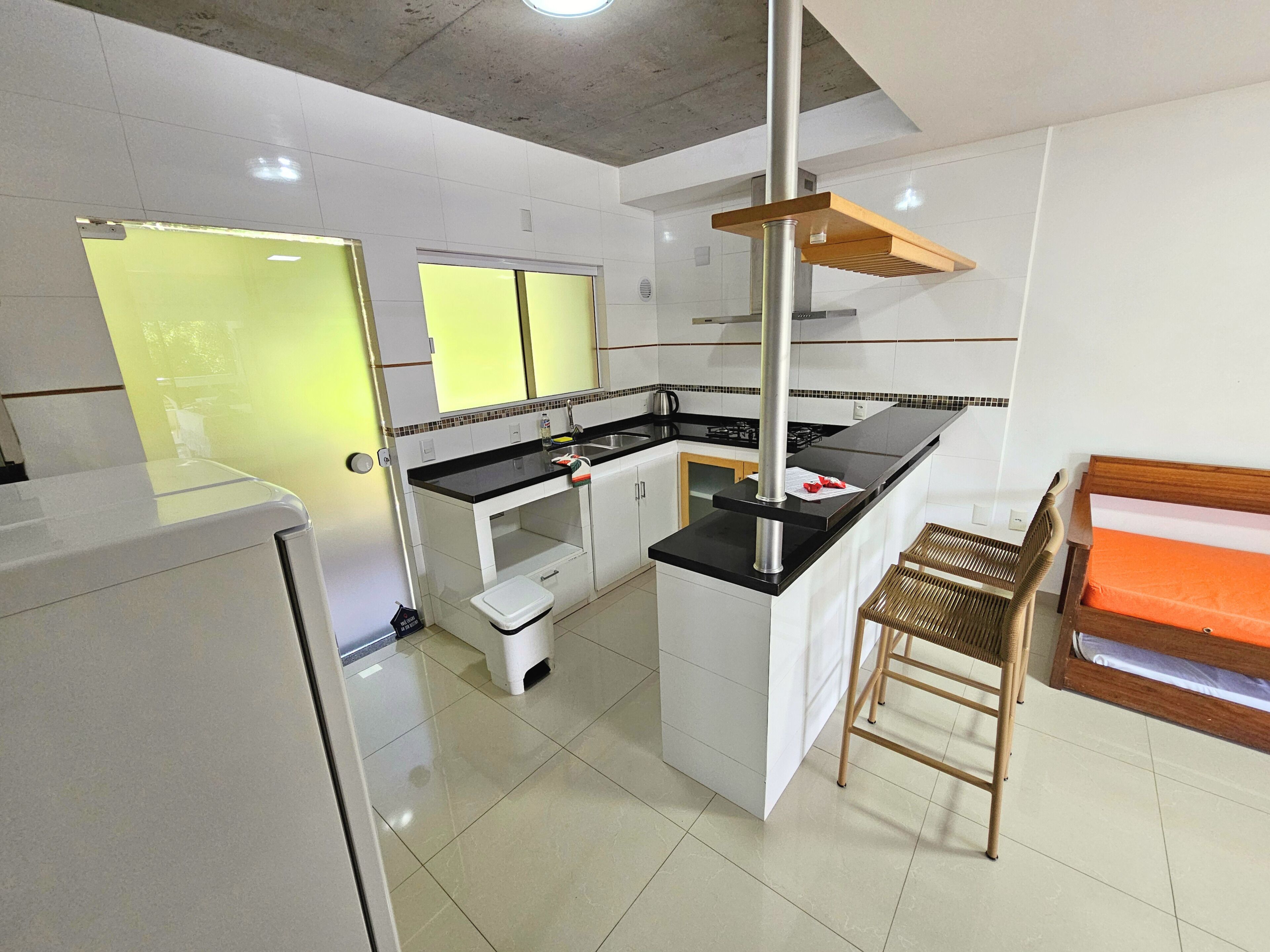 Cozinha moderna com armários brancos, bancada preta e uma cadeira de madeira.
