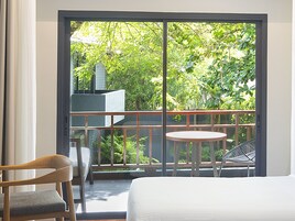 Quarto de hotel com uma grande porta de correr de vidro que dá para uma varanda com vista para o verde.