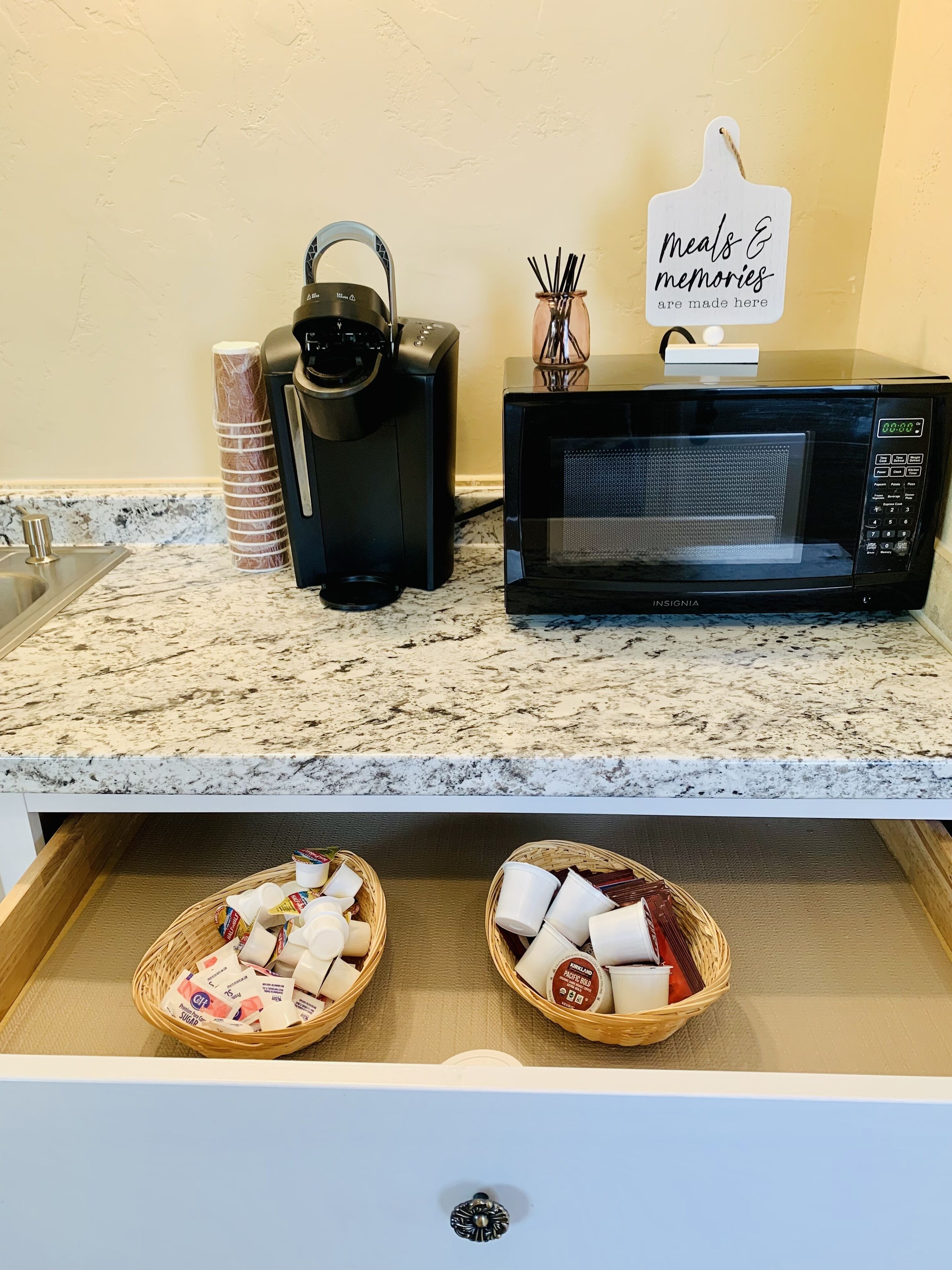Uma bancada de cozinha com micro-ondas, chaleira e uma placa que diz 'lembranças e refeições são feitas aqui'.