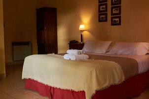 Cama bem arrumada com roupas de cama brancas e bege, abajur e uma pequena mesa com um telefone.