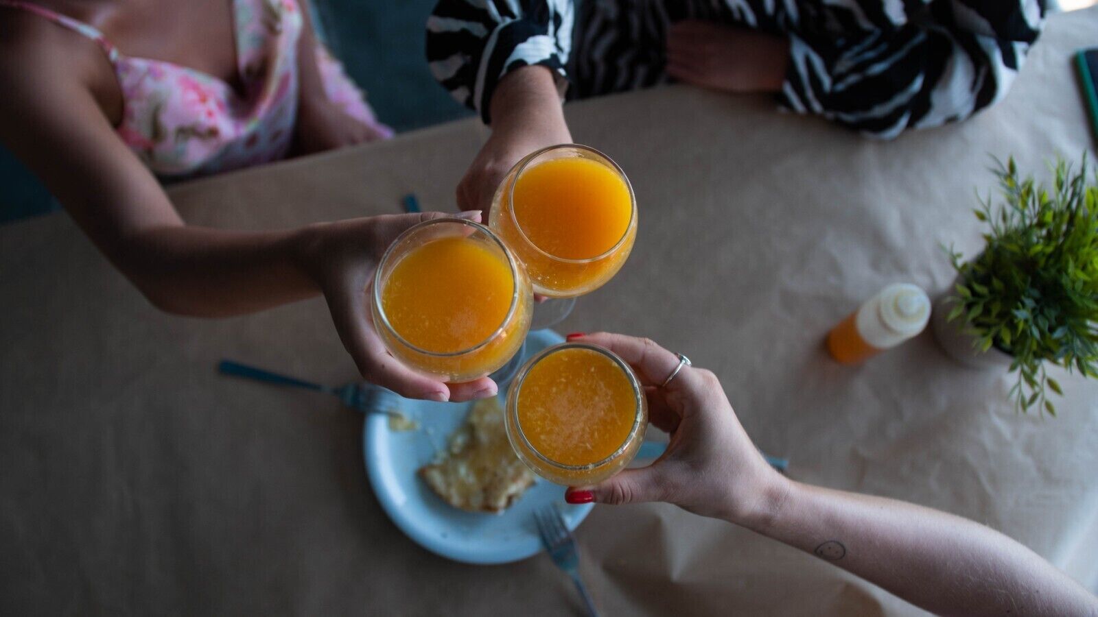 Três pessoas segurando copos de suco de laranja à mesa, com um prato de comida e uma garrafa de molho.