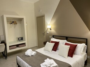 Quarto de hotel com cama, mesa de cabeceira, cadeira, guarda-roupa e espelho.