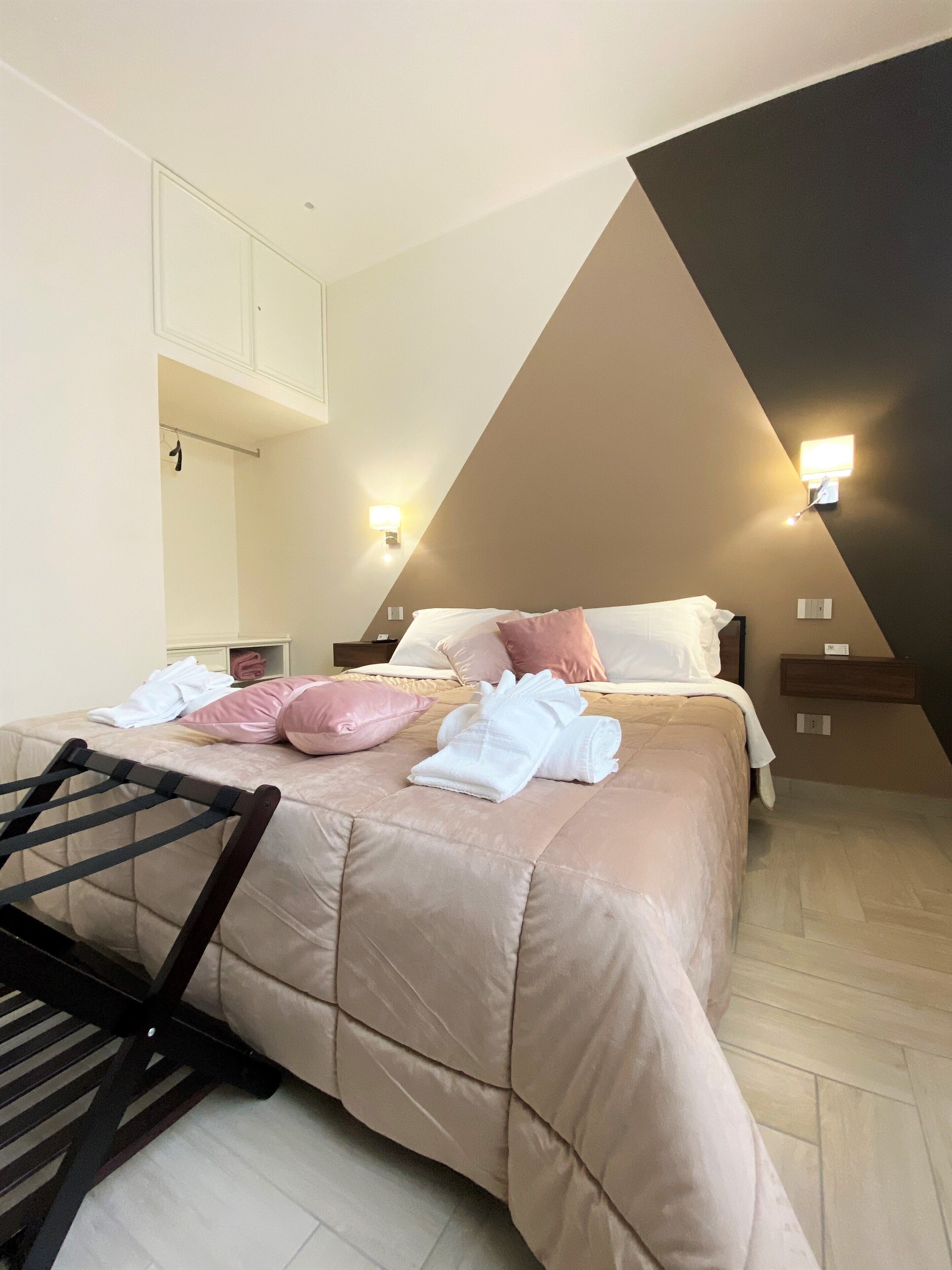 Quarto com cama, almofadas, mesa de cabeceira e luminária fixada na parede.
