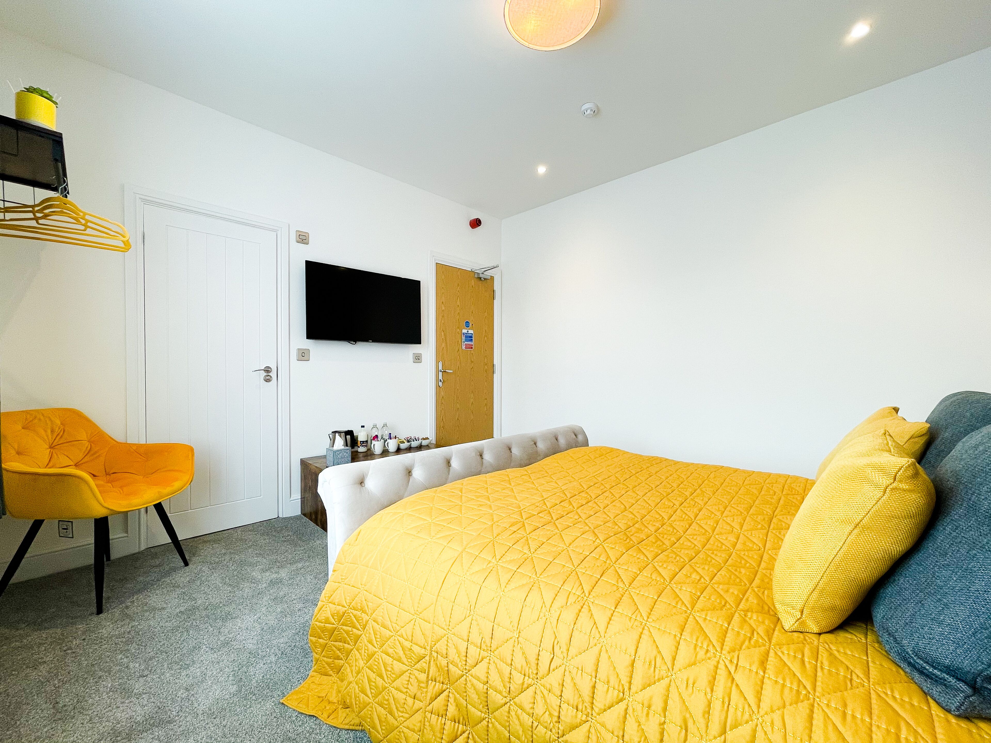 Um quarto com uma cama, uma cadeira, uma televisão e uma porta.