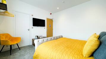 Um quarto com uma cama, uma cadeira, uma televisão e uma porta.