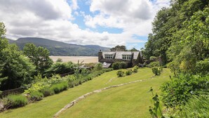 Uma casa de pedra com jardim e vista para um lago e montanhas.