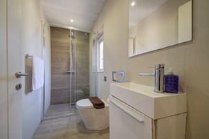 Uma casa de banho moderna com cabine de duche em vidro, lavatório branco e um espelho grande.