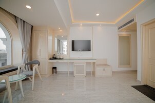 Quarto de hotel moderno com mesa de jantar de vidro, duas cadeiras, TV na parede e uma janela grande com cortinas.