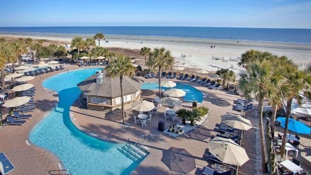 Um resort com piscina, acesso à praia e palmeiras.