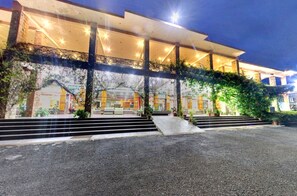 Um edifício moderno com entrada coberta, degraus de acesso e plantas em vasos ao redor.