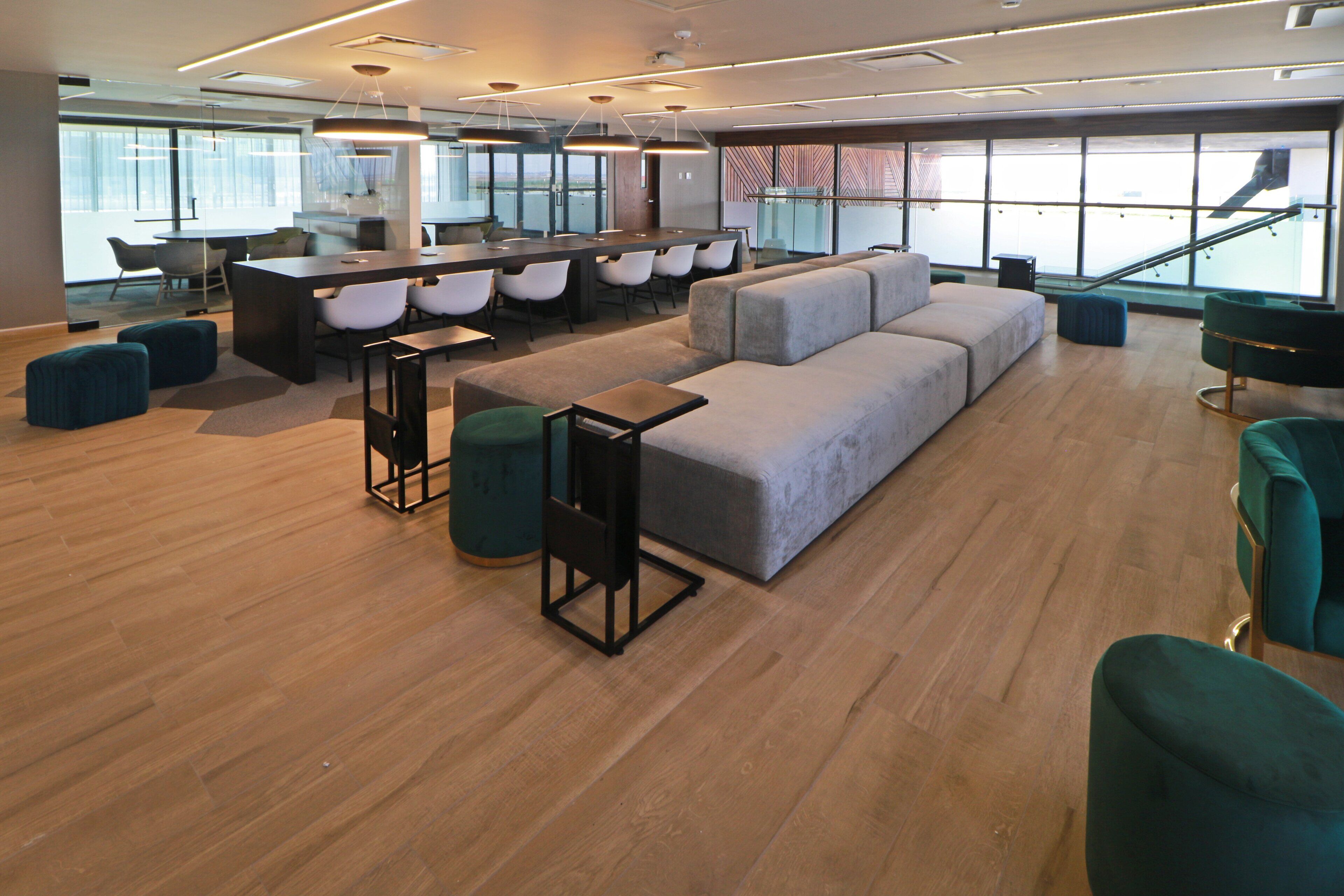 Um espaço de escritório moderno com um amplo sofá cinzento, uma área de bar e uma escadaria.