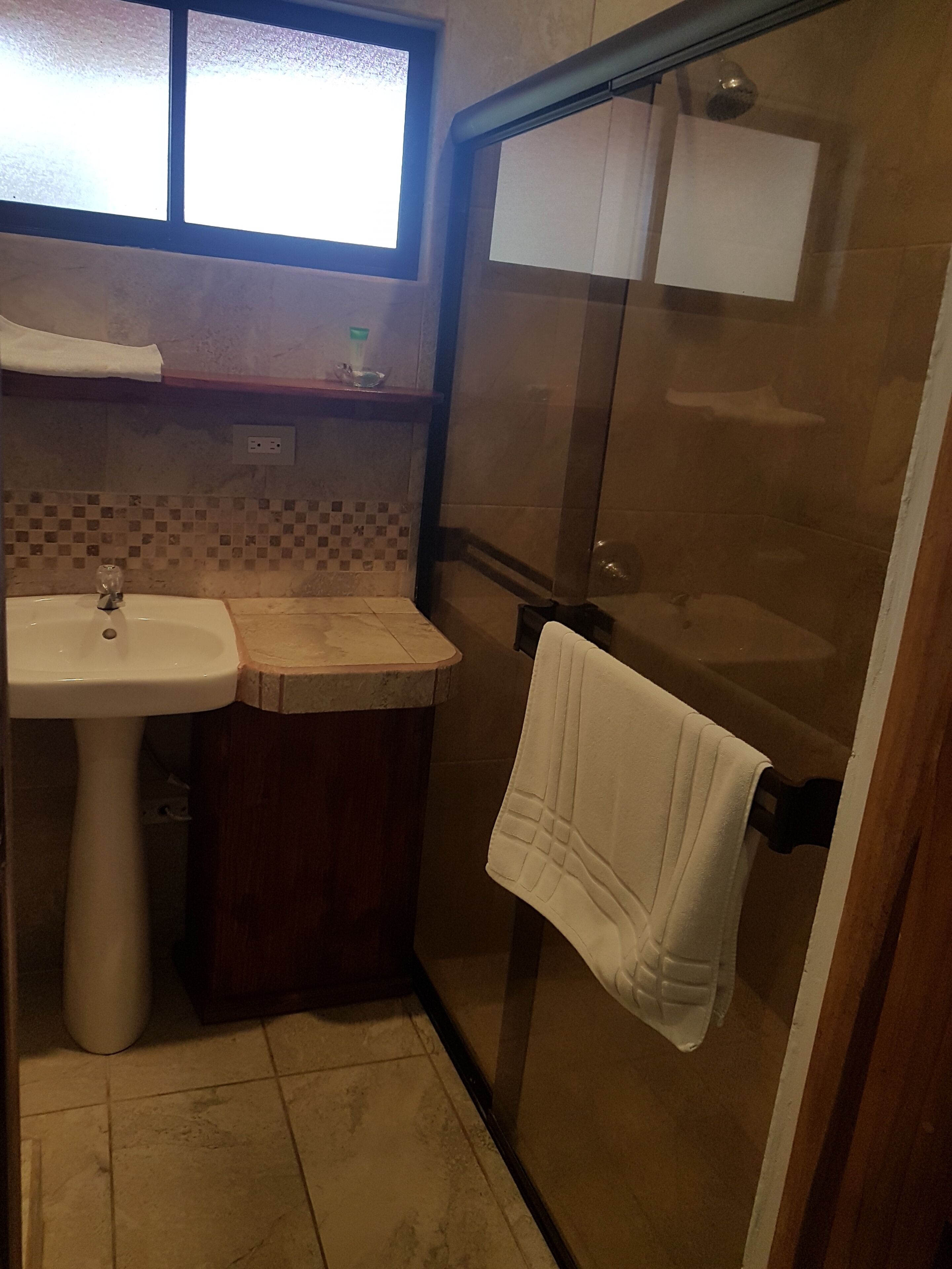 Casa de banho com lavatório, espelho e cabine de duche em vidro.