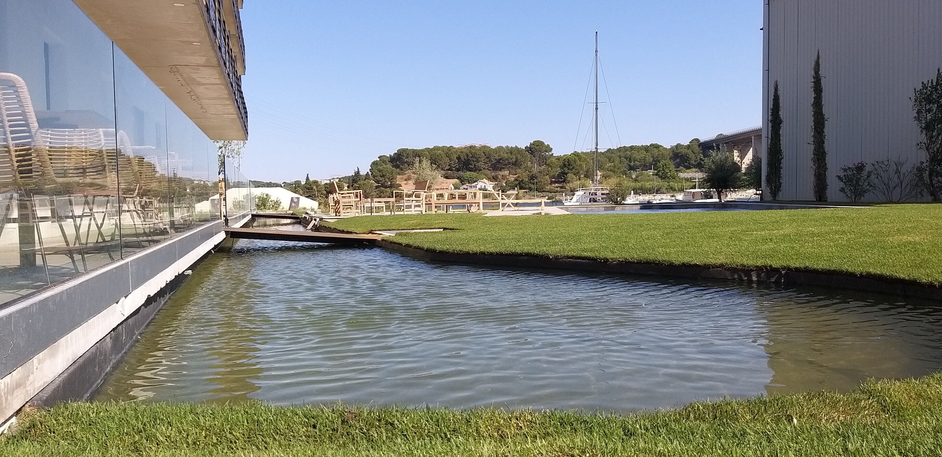 Um canal com uma ponte, uma área gramada e edifícios ao fundo.